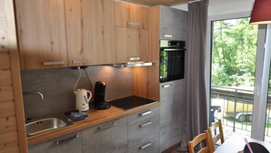 Uma cozinha compacta com armários de madeira, forno embutido, pia e janela com vista para uma varanda.