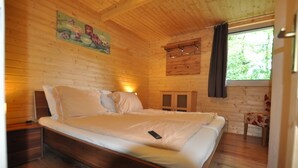 Quarto de cabana de madeira com cama, mesa de cabeceira, cadeira e janela.
