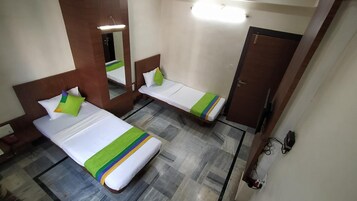 Quarto de hotel com duas camas de solteiro, cada uma com colcha verde e branca listrada, cabeceira de madeira e espelho sobre a cama.