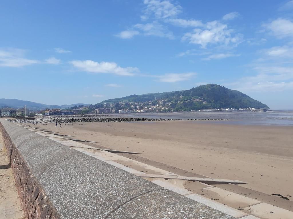 Uma praia costeira com um muro de pedra e uma colina ao longe.