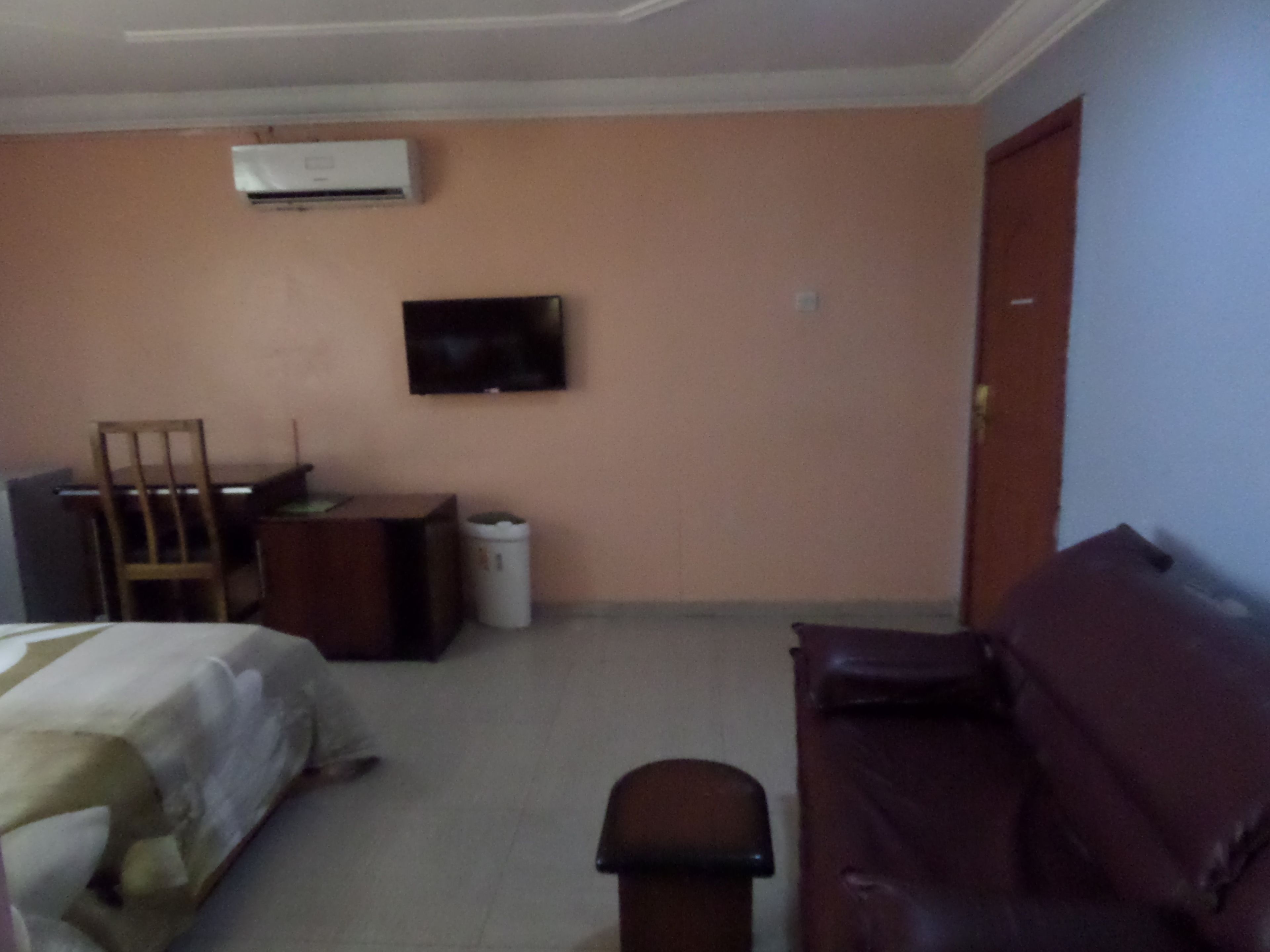 Quarto com uma cama, escrivaninha, cadeira, televisão e porta.