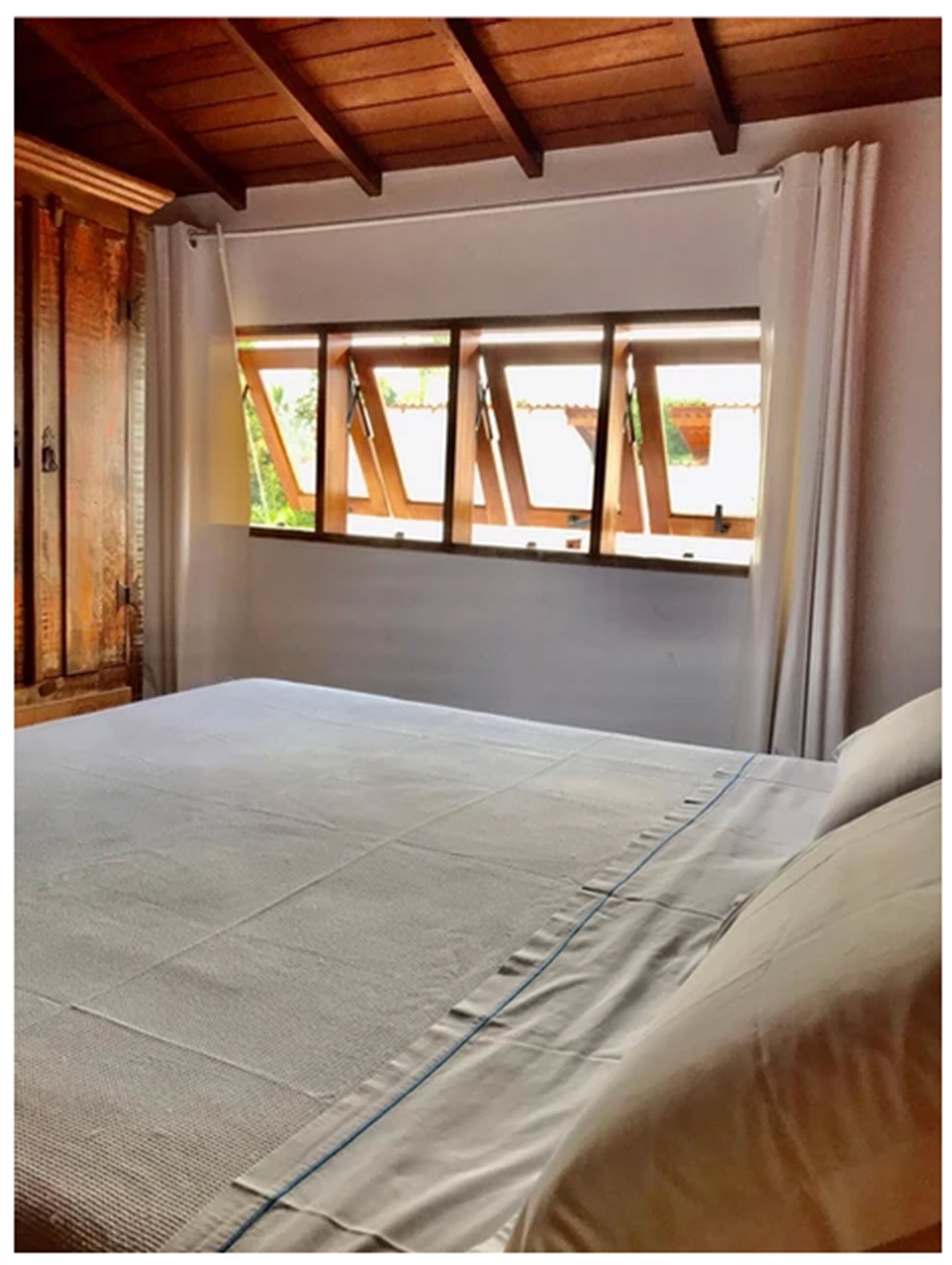 Um quarto com cama, vigas de madeira no teto e janela com cortinas.