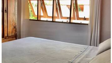 Um quarto com cama, vigas de madeira no teto e janela com cortinas.