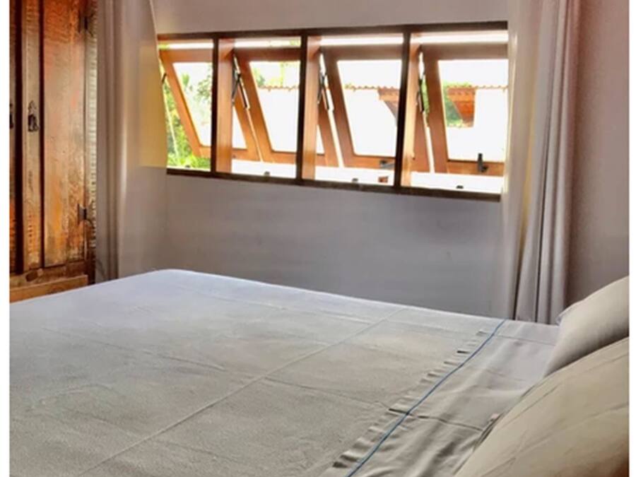 Um quarto com cama, vigas de madeira no teto e janela com cortinas.
