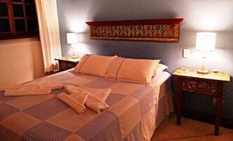Uma cama bem arrumada com manta listrada, duas mesas de cabeceira com abajures e um adorno na parede acima da cama.