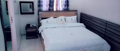 Quarto com cama, mesa de cabeceira, uma pequena mesa e ar condicionado na parede.