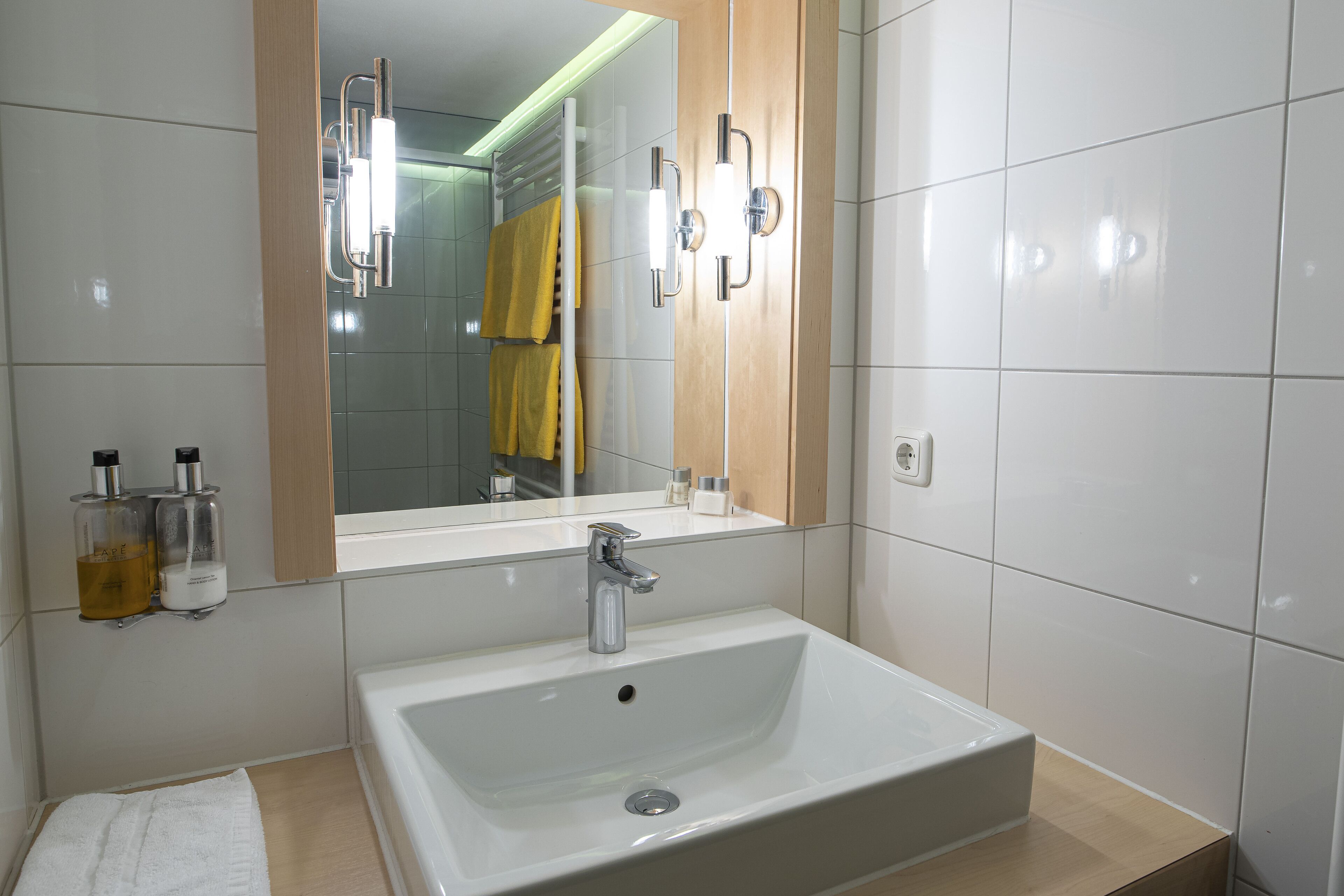 Casa de banho moderna com lavatório branco, espelho e porta-toalhas.