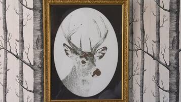 Obra de arte emoldurada de cabeça de veado numa parede com padrão de árvore.