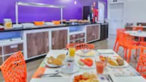 Uma sala de jantar moderna com cadeiras laranja vibrantes, parede roxa e um balcão com alimentos.