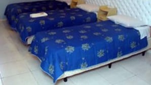 Quarto com duas camas, ventilador no teto e parede de destaque laranja.