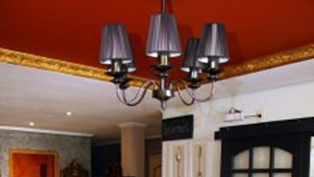 Uma sala de jantar com chão xadrez, uma mesa de madeira com cadeiras, um lustre e uma porta com padrão de grade.