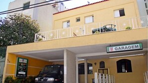 Um edifício com fachada amarela, uma placa indicando garagem, e um carro preto estacionado em frente.