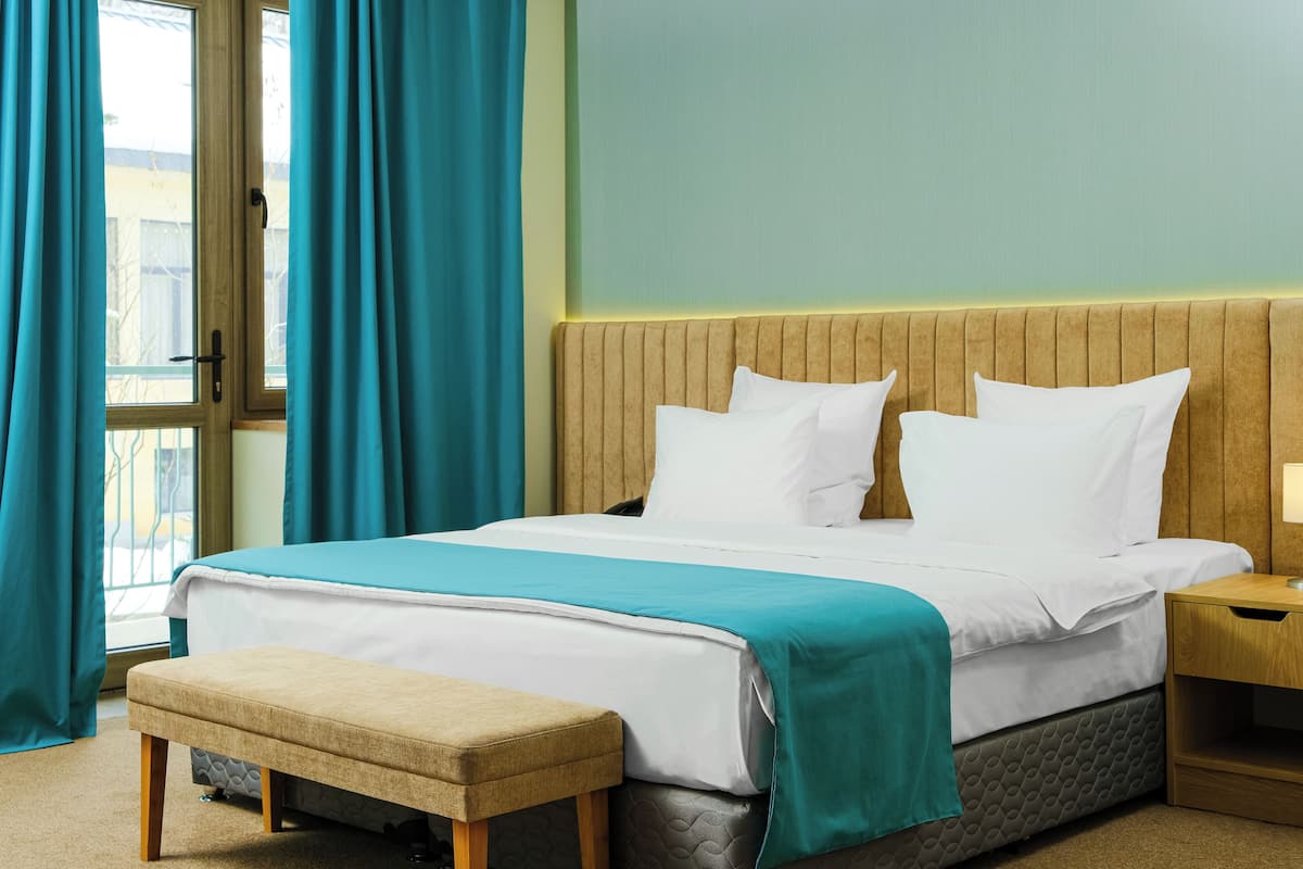 Cama bem arrumada com colcha verde-água, cabeceira de madeira e mesa de cabeceira com abajur.
