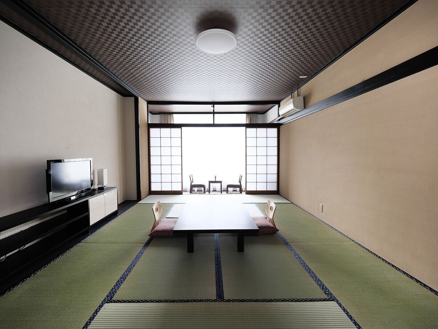 Um quarto japonês tradicional com tatames, uma mesa baixa, cadeiras e uma televisão.