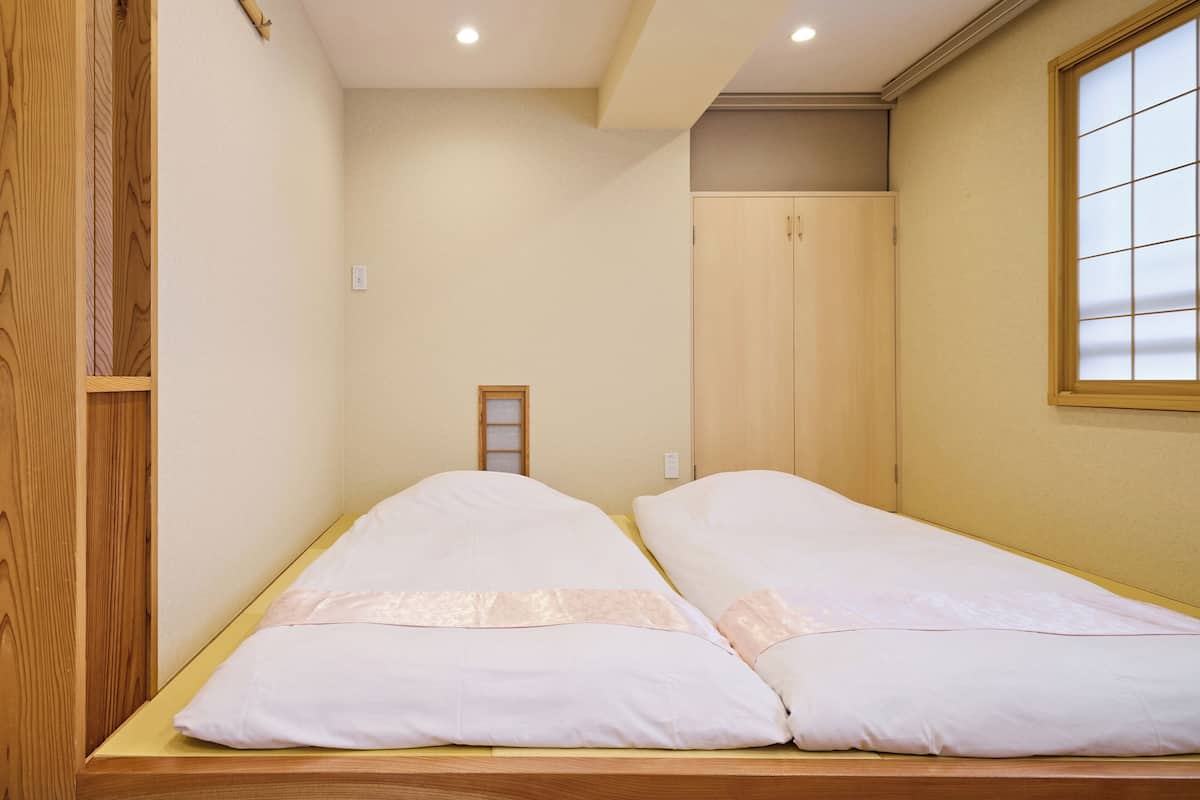 Quarto com duas camas, guarda-roupa de madeira e uma janela.