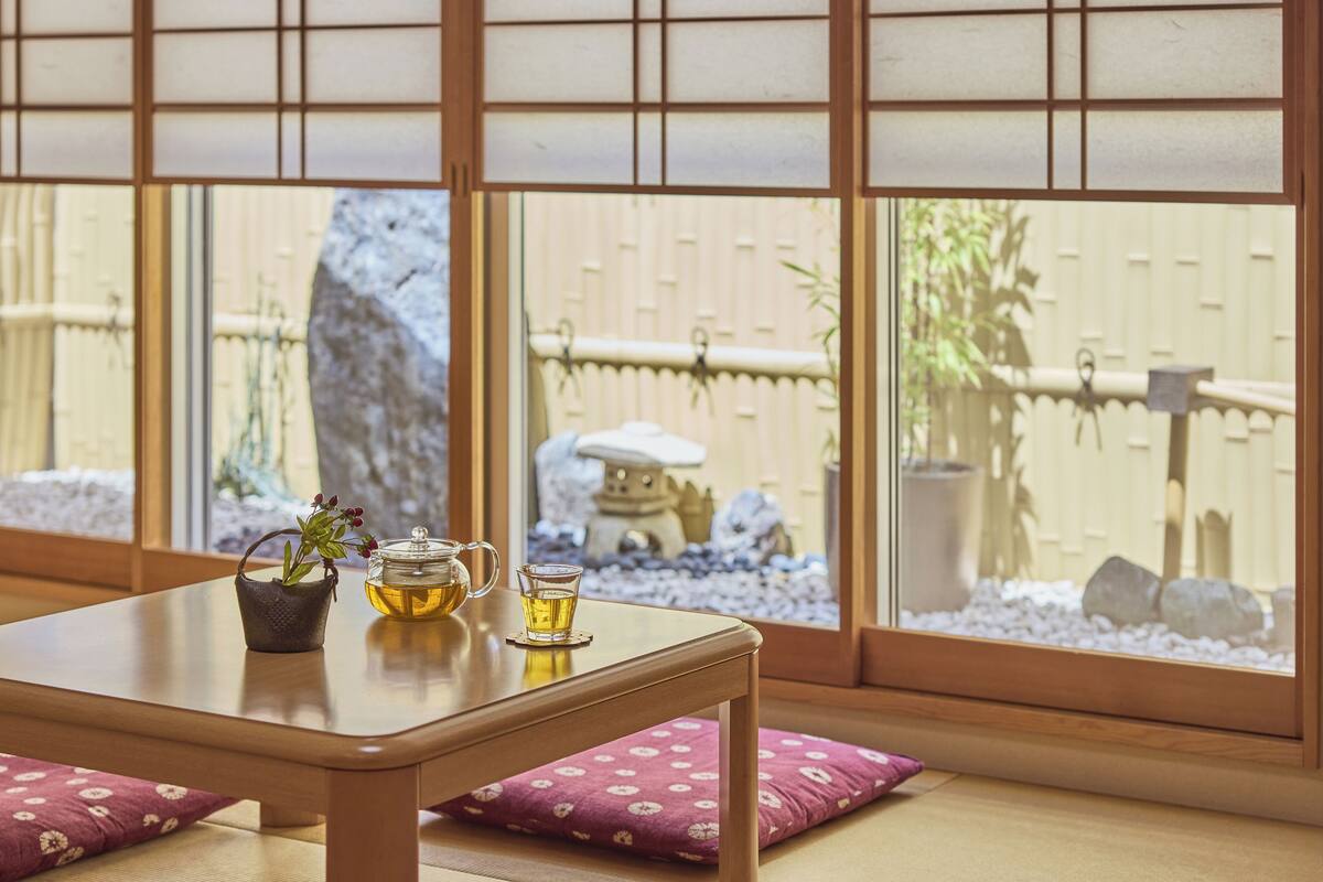 Um quarto japonês tradicional com tatames, uma mesa de madeira baixa e vista para um jardim através de biombos shoji.