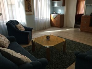 Uma sala de estar com sofá, mesa de centro e área de cozinha com armários e um relógio.