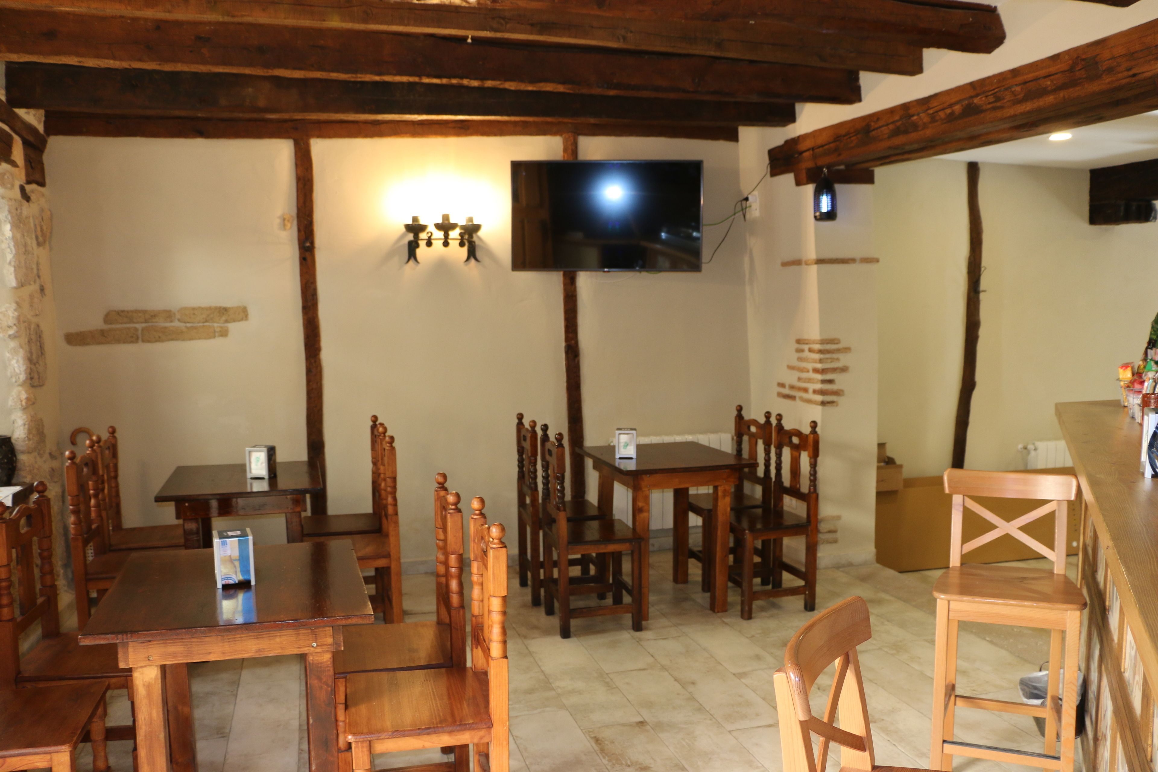 Uma sala de jantar com mesas e cadeiras de madeira, uma televisão fixada na parede e teto de madeira.