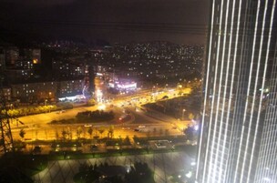 Paisagem urbana noturna com edifícios iluminados e um cruzamento movimentado.