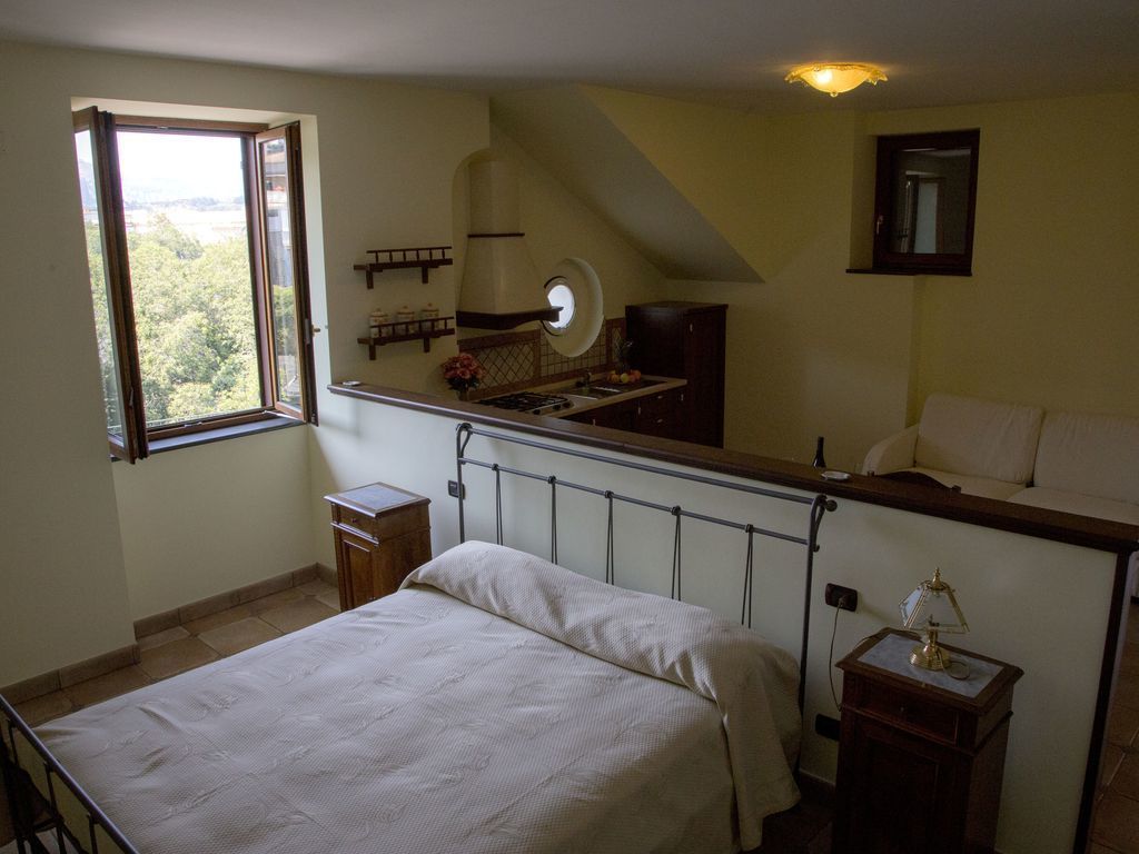 Um quarto com cama, janela, uma mesinha e criado-mudo.