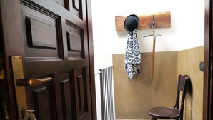 Um quarto com porta de madeira, uma cadeira, um cabideiro com chapéu e uma espada.