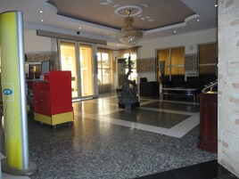 Um hall com chão xadrez, balcão de recepção, um lustre e uma estátua.