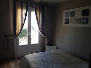 Quarto com cama, cortinas, radiador e uma parede com quadros.