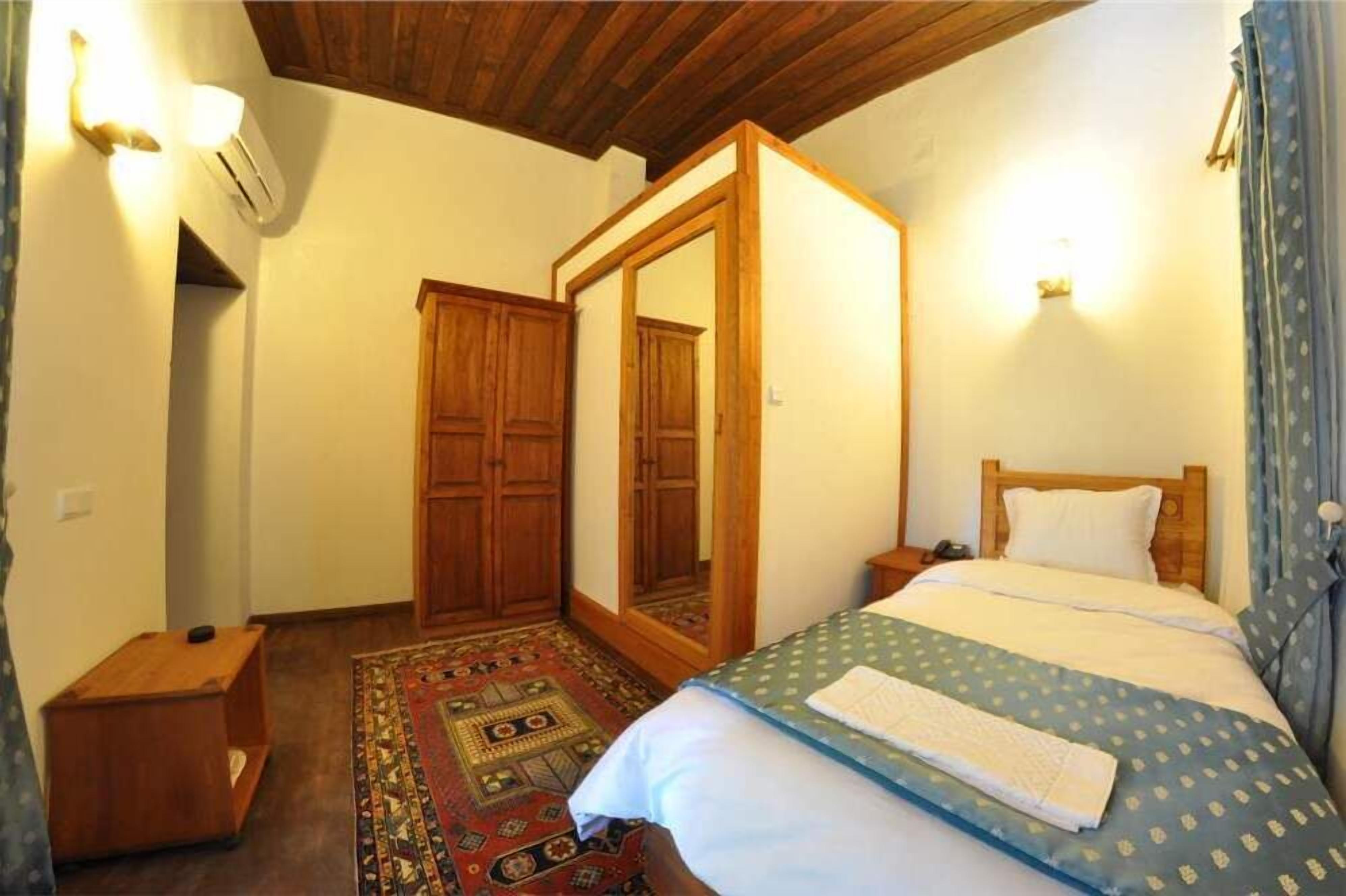 Quarto com guarda-roupa de madeira, cama com colcha estampada e uma pequena mesa de cabeceira de madeira.