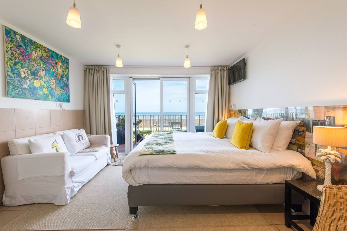 Quarto de hotel com uma cama, um sofá, um quadro e vista para o mar.