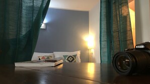 Um quarto com uma cama, uma luminária de cabeceira, uma câmera Nikon e um livro sobre uma mesa.
