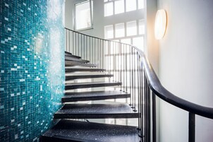 Escada com parede revestida de azulejos de um lado e luminária do outro.