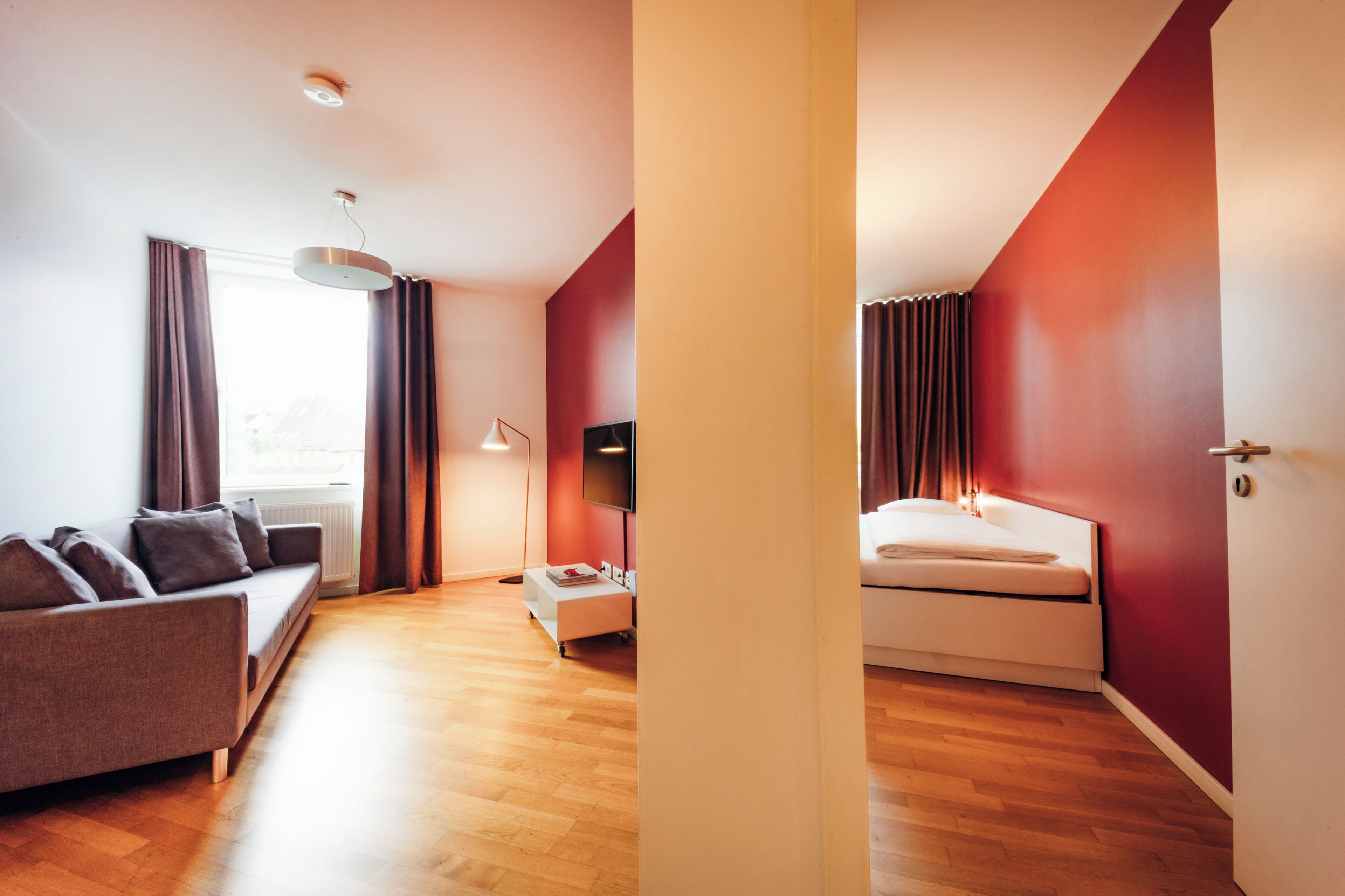Quarto de hotel moderno com sofá, mesa de cabeceira, televisão de tela plana e uma cama.