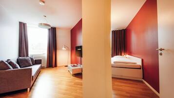 Quarto de hotel moderno com sofá, mesa de cabeceira, televisão de tela plana e uma cama.
