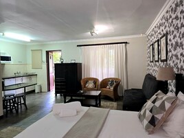 Quarto de hotel com cama, mesa de jantar, cozinha e sala de estar com sofá e poltronas.