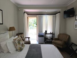 Quarto de hotel com cama, poltrona, televisão, cafeteira e janela com cortinas.
