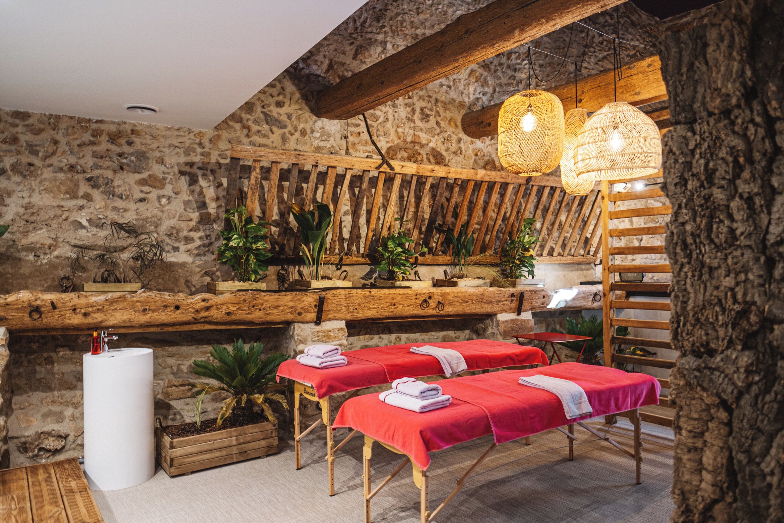 Um espaço de spa com vigas de madeira, paredes de pedra e duas mesas de massagem com toalhas.