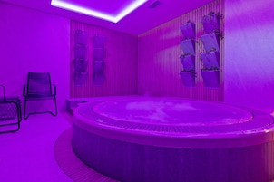 Um spa moderno com banheira de hidromassagem circular, painéis de jardim vertical e uma cadeira preta.