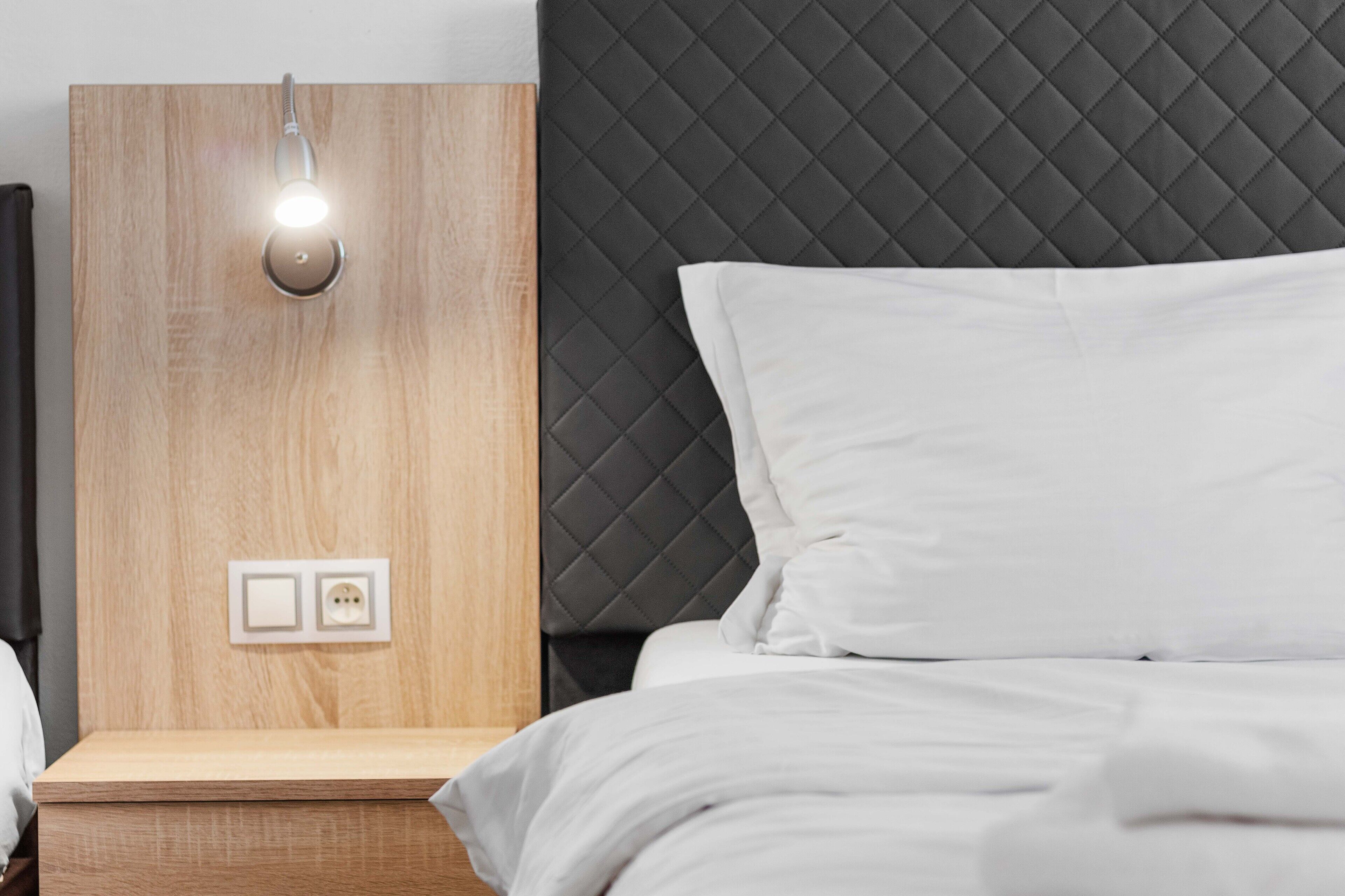 Quarto moderno com cabeceira de madeira, mesa de cabeceira e cama com roupa de cama branca.