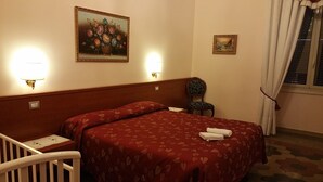 Quarto de hotel com cama, uma cadeira, mesa de cabeceira, abajur e duas pinturas na parede.