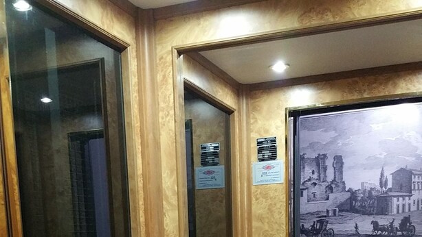 Um elevador com design em painel de madeira, painel de controle com botões e um espelho refletindo um edifício histórico e a paisagem urbana.