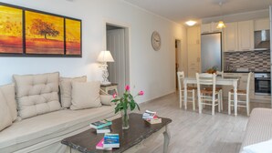 Uma sala de estar com um sofá, mesa de centro com livros, um vaso com flores e um quadro na parede.