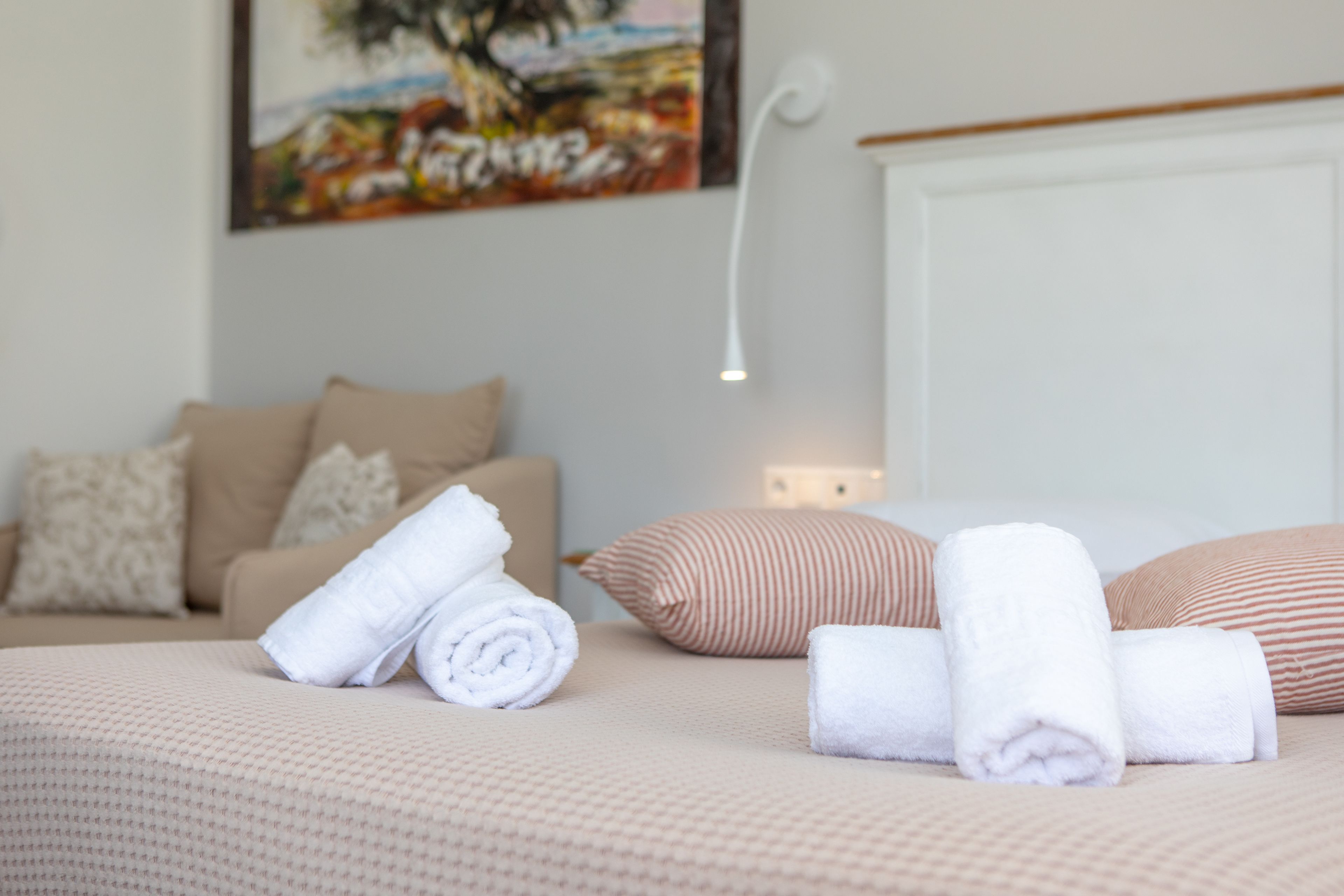 Cama bem arrumada com toalhas brancas dobradas, um sofá bege com almofadas estampadas e um quadro na parede.