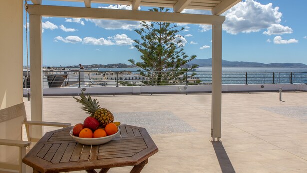 Uma mesa com uma tigela de frutas e vista para o mar e montanhas.