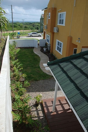 Área residencial com gramado bem cuidado, um caminho que leva a uma casa com telhado verde e um carro estacionado ao fundo.