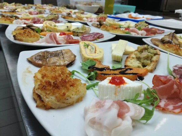 Buffet com diversos pratos, incluindo pães, queijos e carnes.