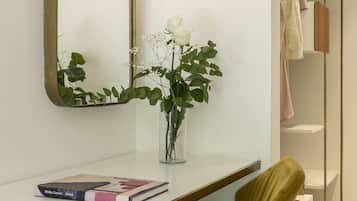 Quarto moderno com escrivaninha branca, espelho, cadeira verde e um vaso com flores.