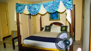 Uma cama com estrutura de madeira, um ventilador de cabeceira e uma cadeira.