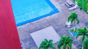 Vista aérea de uma área de piscina com pista vermelha, cadeiras de descanso e palmeiras.