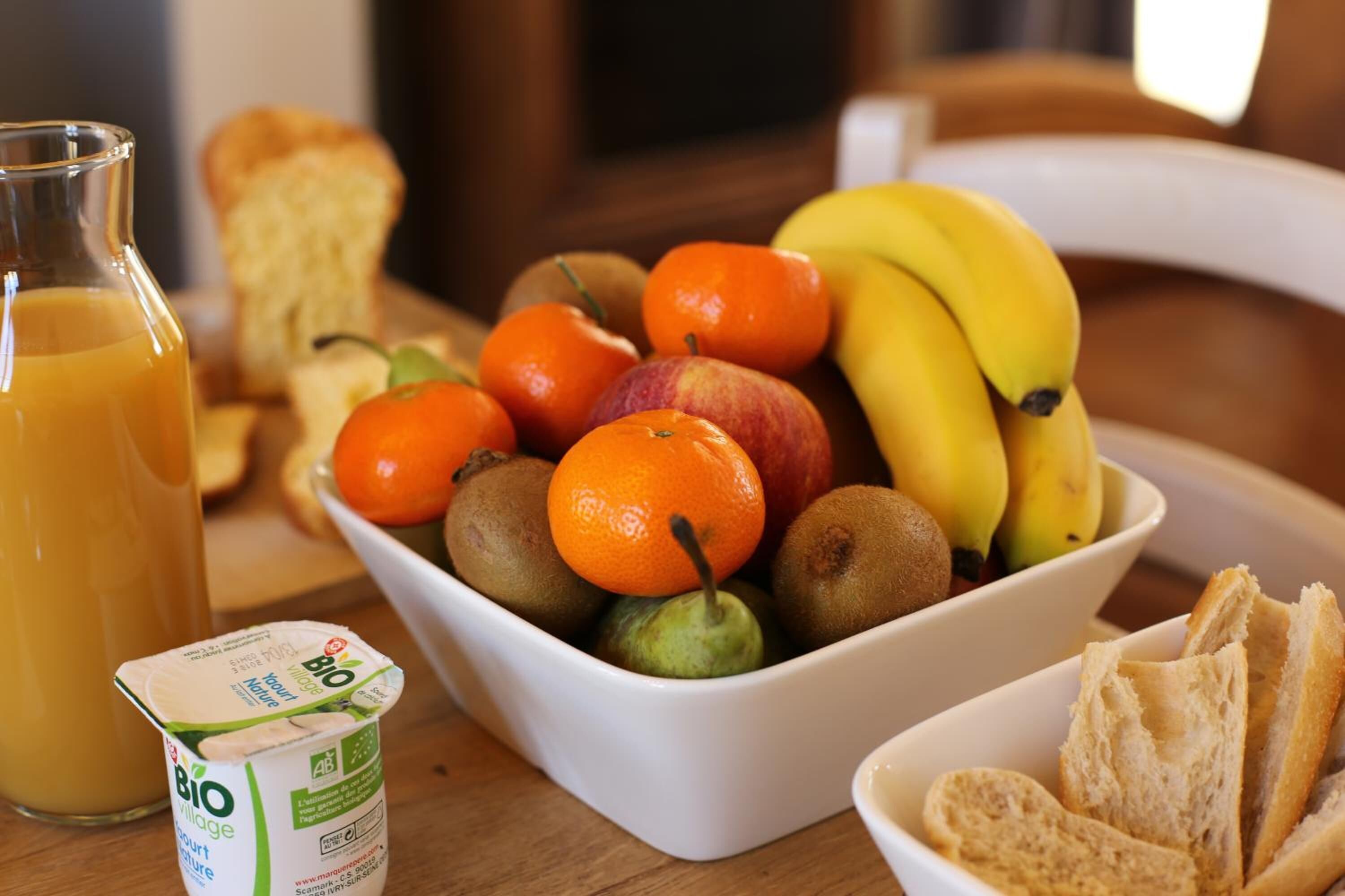 Uma mesa de café da manhã com uma tigela de frutas, um copo de suco de laranja e um pote de iogurte.