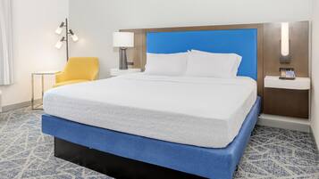 Quarto de hotel com cama grande, mesa de cabeceira com luminária, cadeira e telefone fixado na parede.
